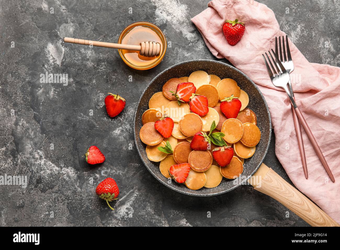 Composition with frying pan of mini pancakes, strawberry and honey on ...