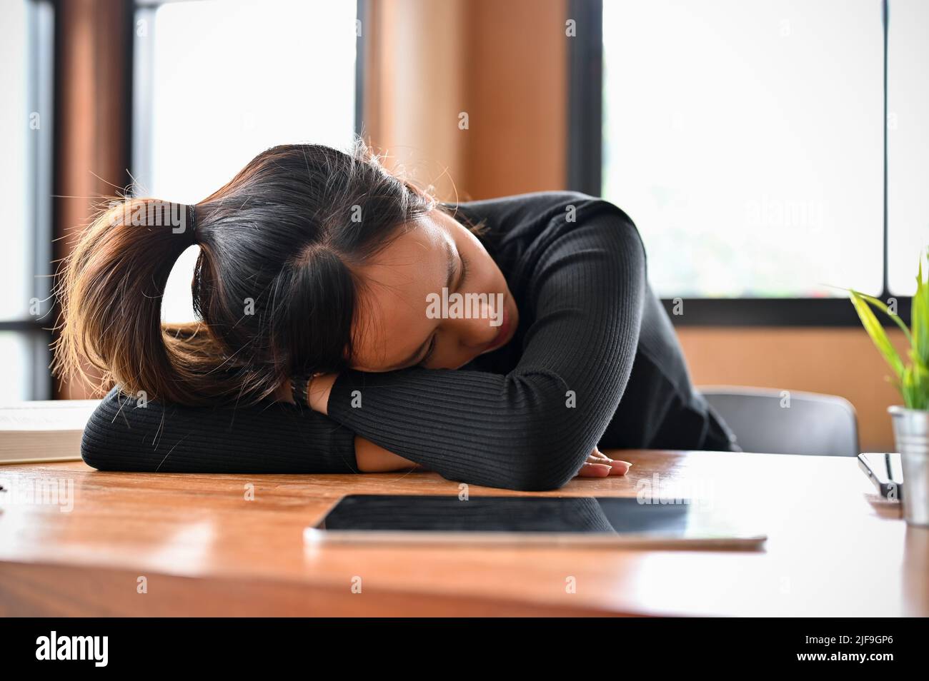 Tired sleepy young Asian female worker or college student sleeping on the desk. Exhausted from ...