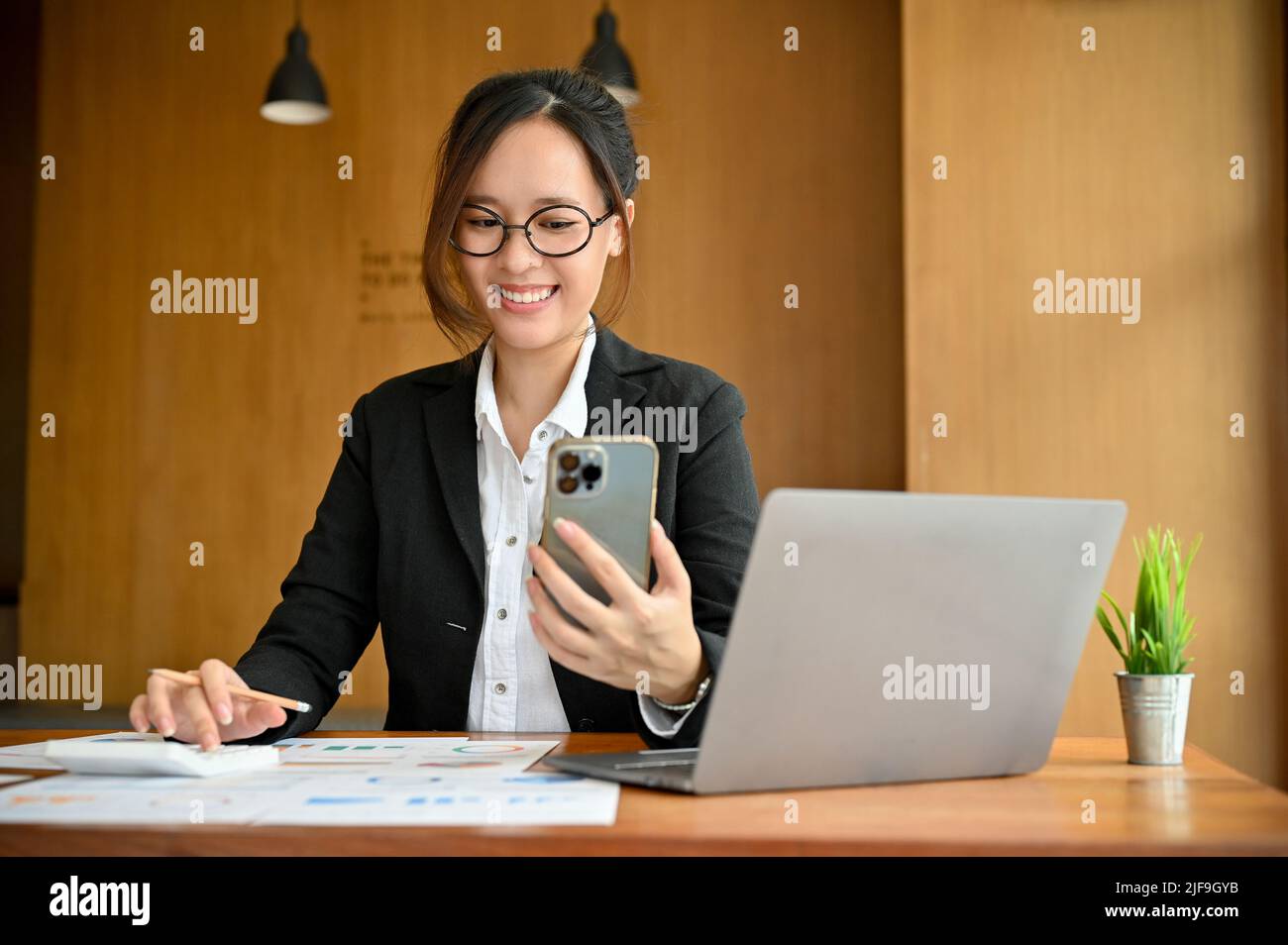 Pretty young Asian female accountant with eyeglasses sits at her office ...