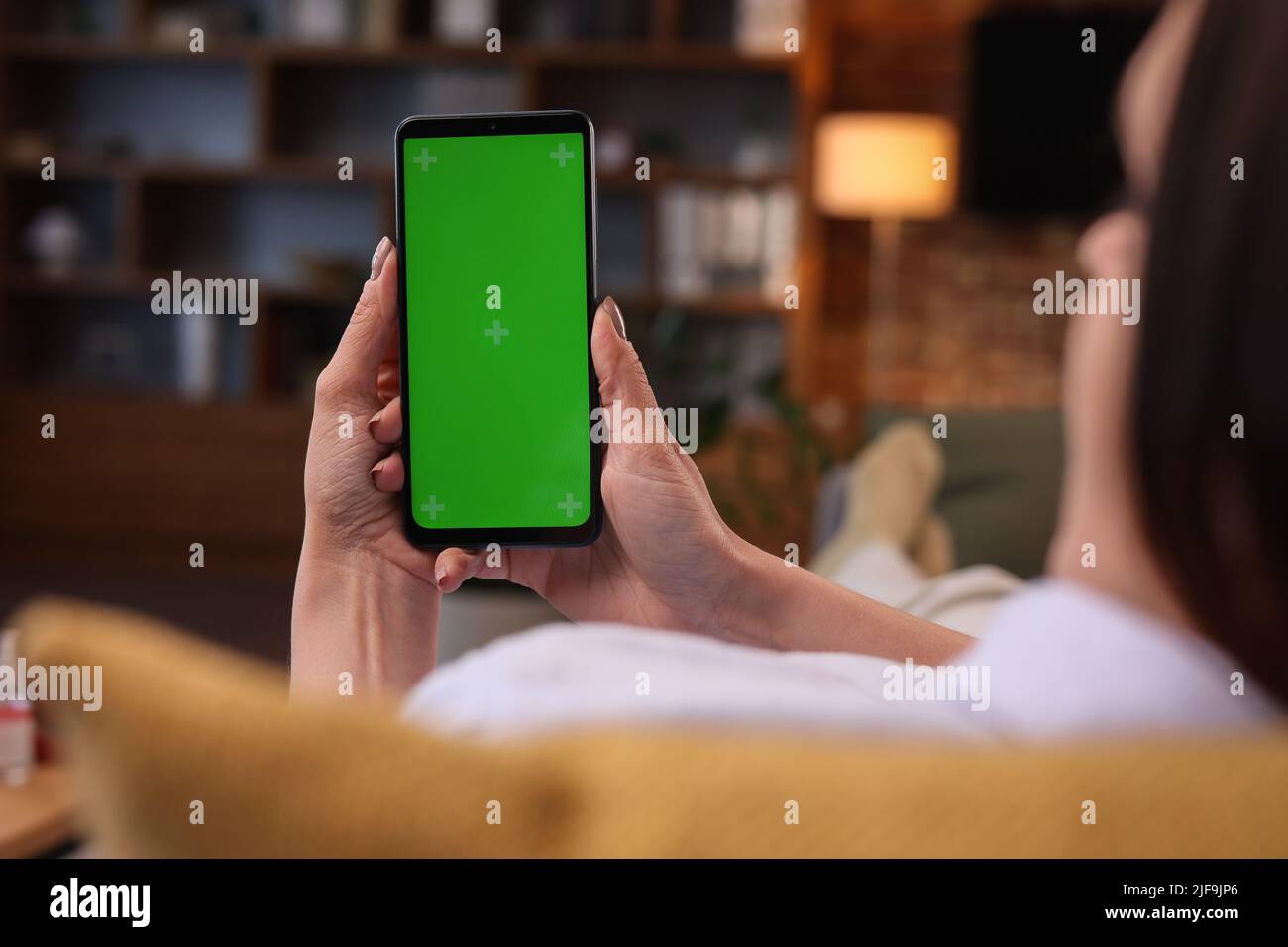Over shoulder view of young woman holding smartphone with green mock-up ...