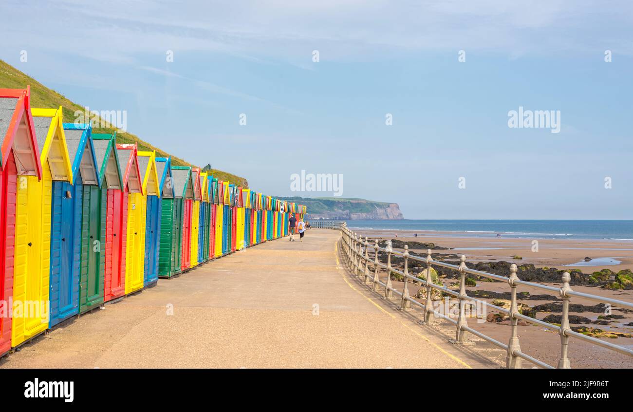 A line of colourful beach huts beside a beach at low tide. There is a ...