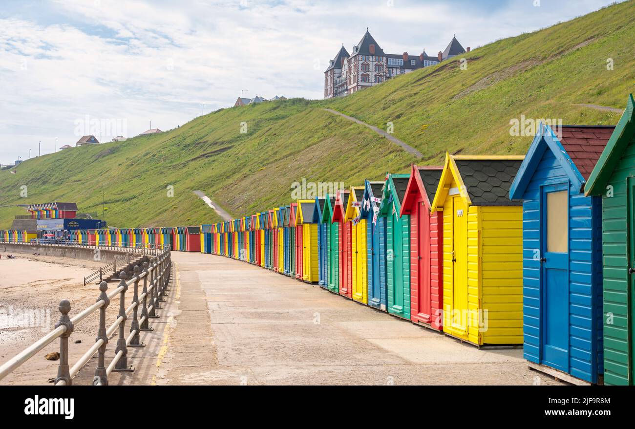 A line of colourful beach huts beside a sandy beach. A path leads ...