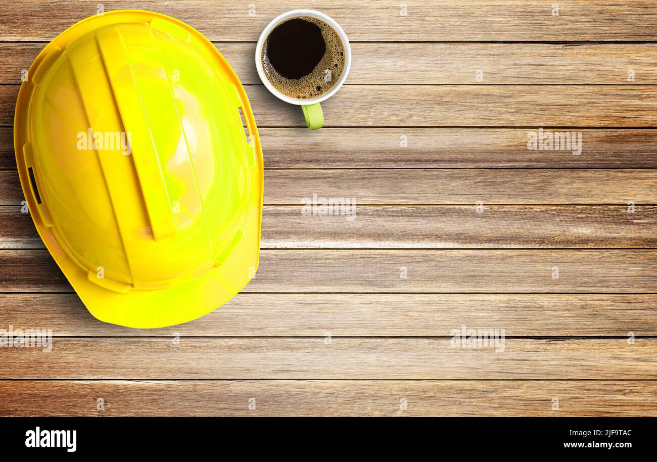 Top view yellow safety helmet and cup of coffee on wood table ...