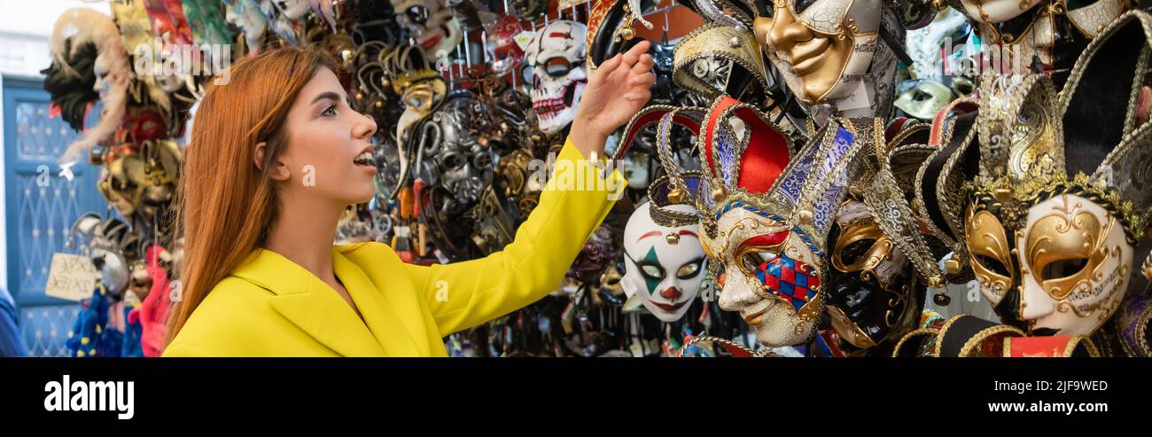 amazed redhead woman choosing colorful carnival mask in Venice, banner ...