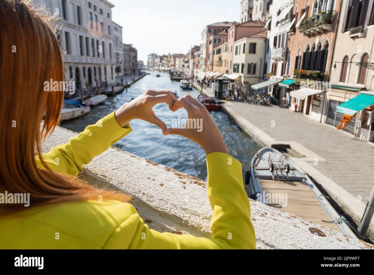 partial view of redhead woman showing heart sign over blurred Grand ...