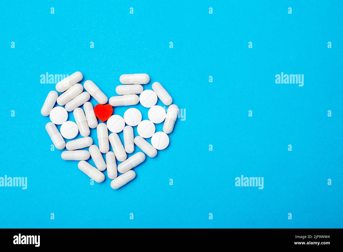 Red pill in the shape of a heart on the background of white pills and a ...