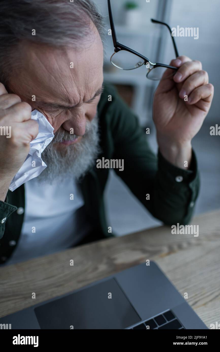 high angle view of bearded senior man holding eyeglasses and crumpled ...
