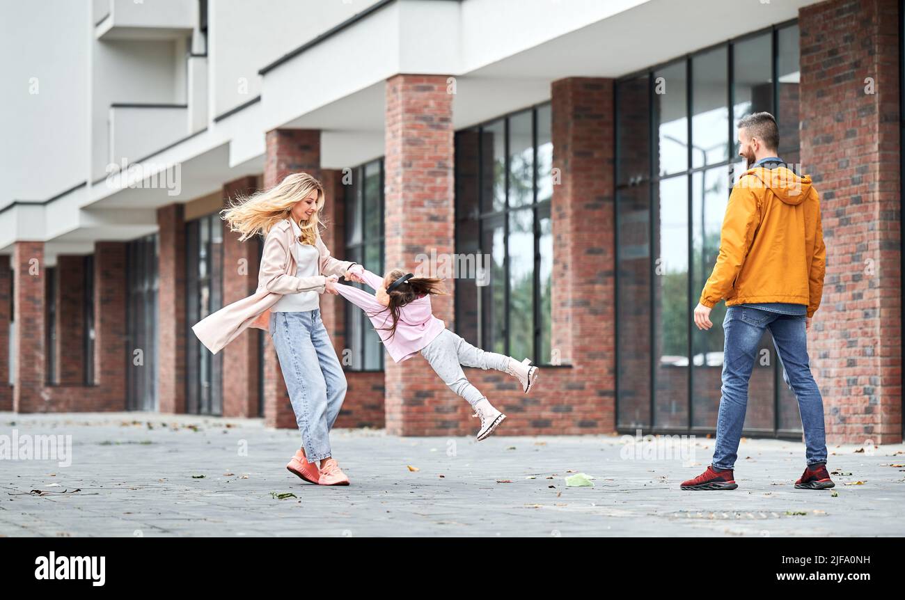 Full length of smiling blonde woman spinning daughter holding kid hands ...