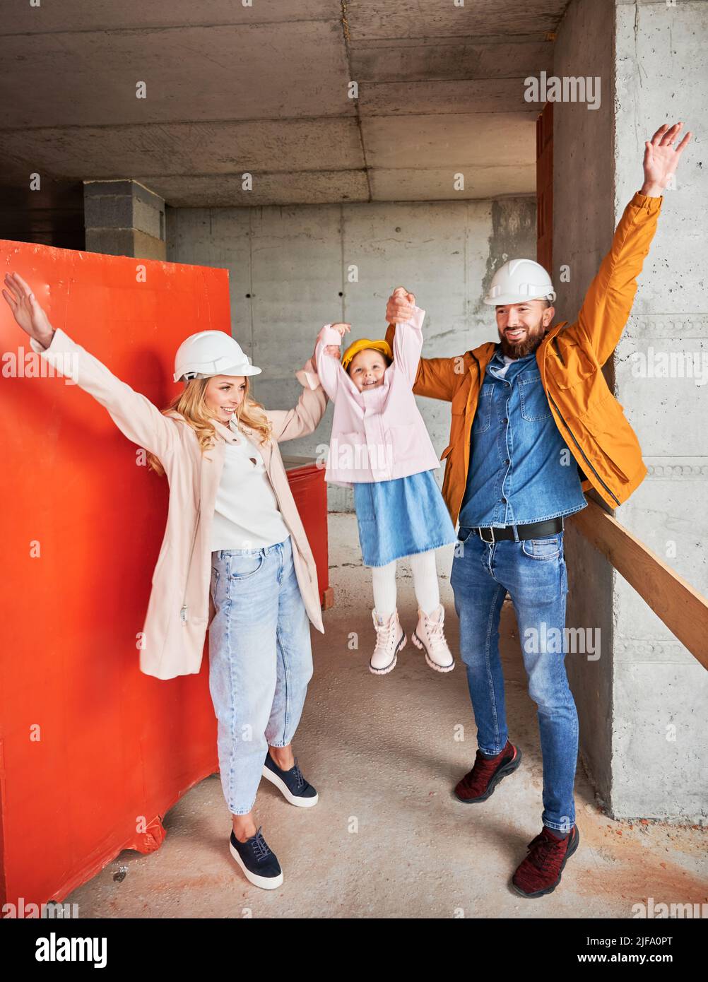 Full length of parents raising hands and smiling while holding daughter ...