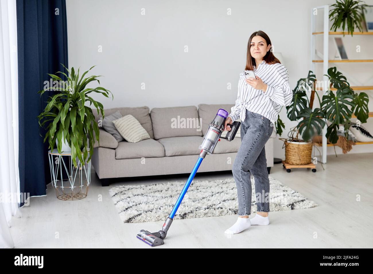 Happy cheerful young Caucasian beautiful woman vacuuming floor and ...