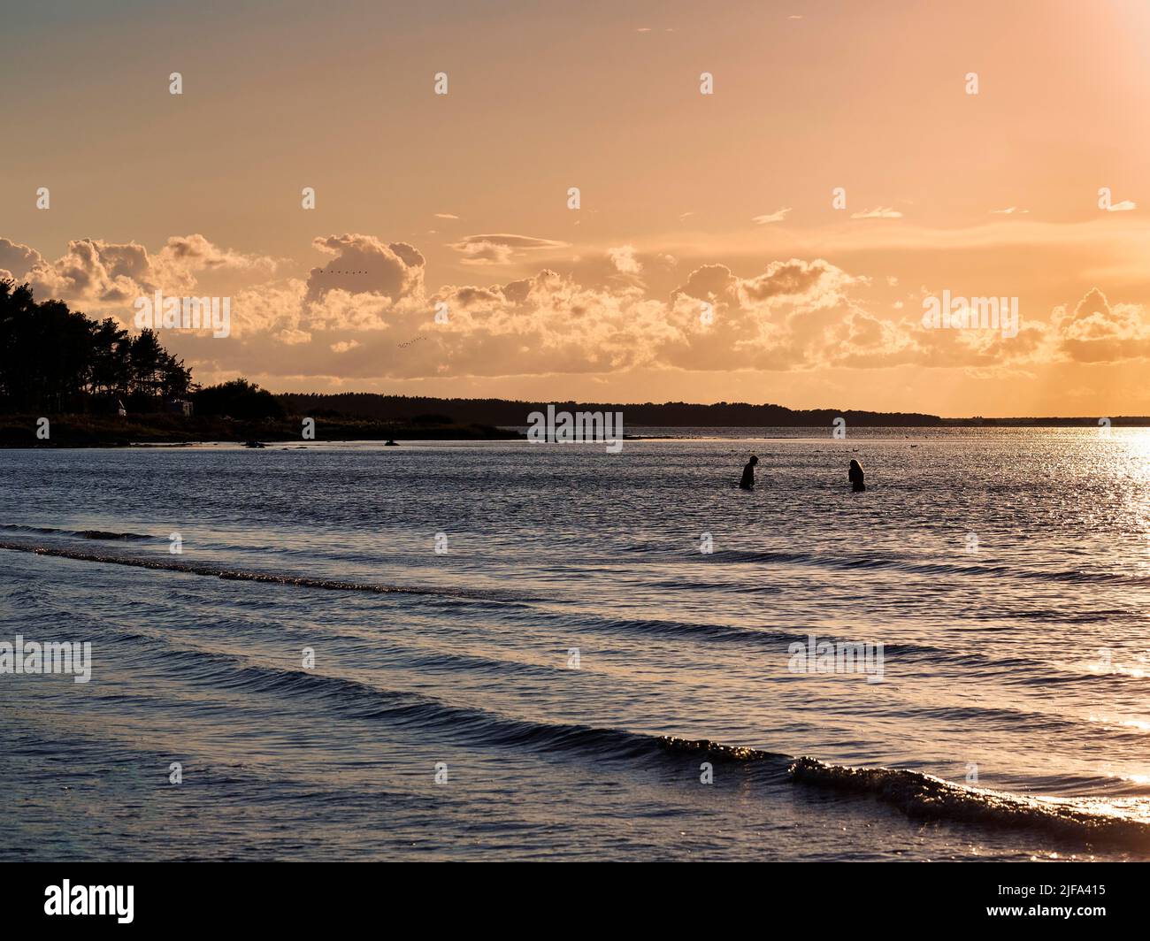Two people, silhouettes in the sea, enjoying evening sun, summer sunset ...