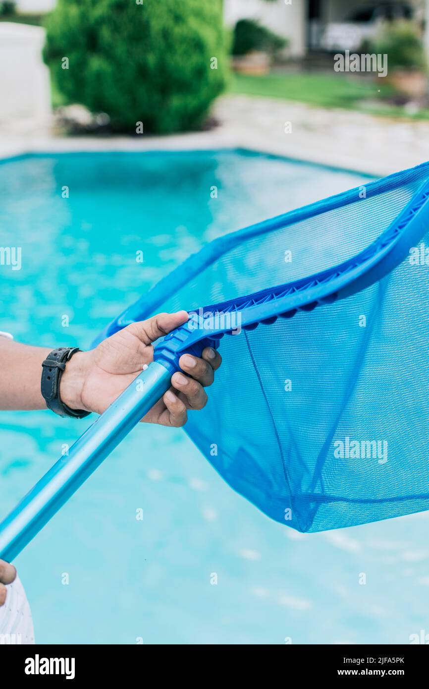 Hands holding a skimmer with blue pool in the background, A man ...