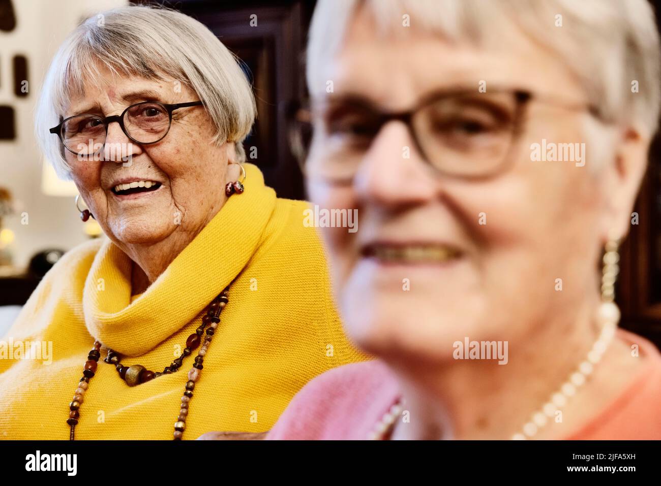 Two senior citizens, sisters, laughing friendly into the camera at home ...