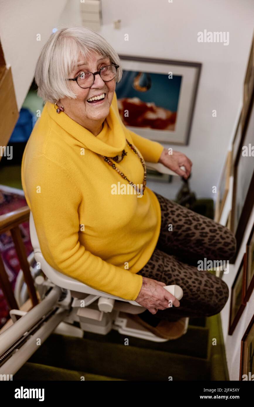 Senior woman laughing at home riding the stair lift up the stairs ...