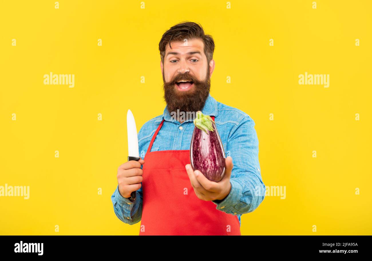Happy guy in apron looking at eggplant holding chefs knife yellow ...