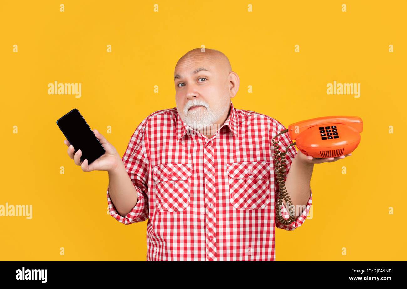 confused old man with retro telephone and modern smartphone on yellow ...