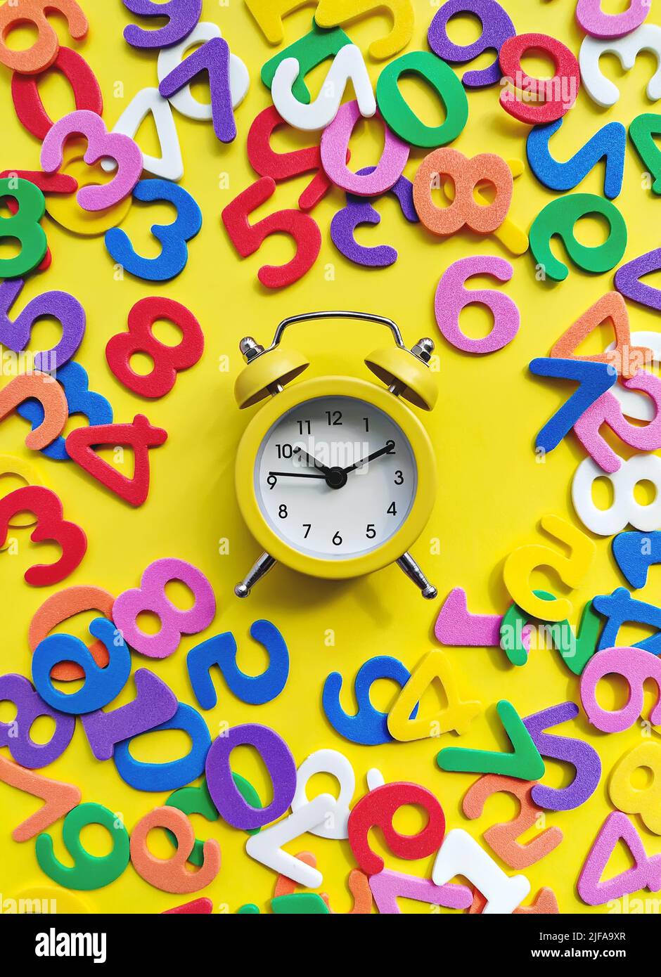 Illuminated yellow alarm clock on yellow background with colorful ...