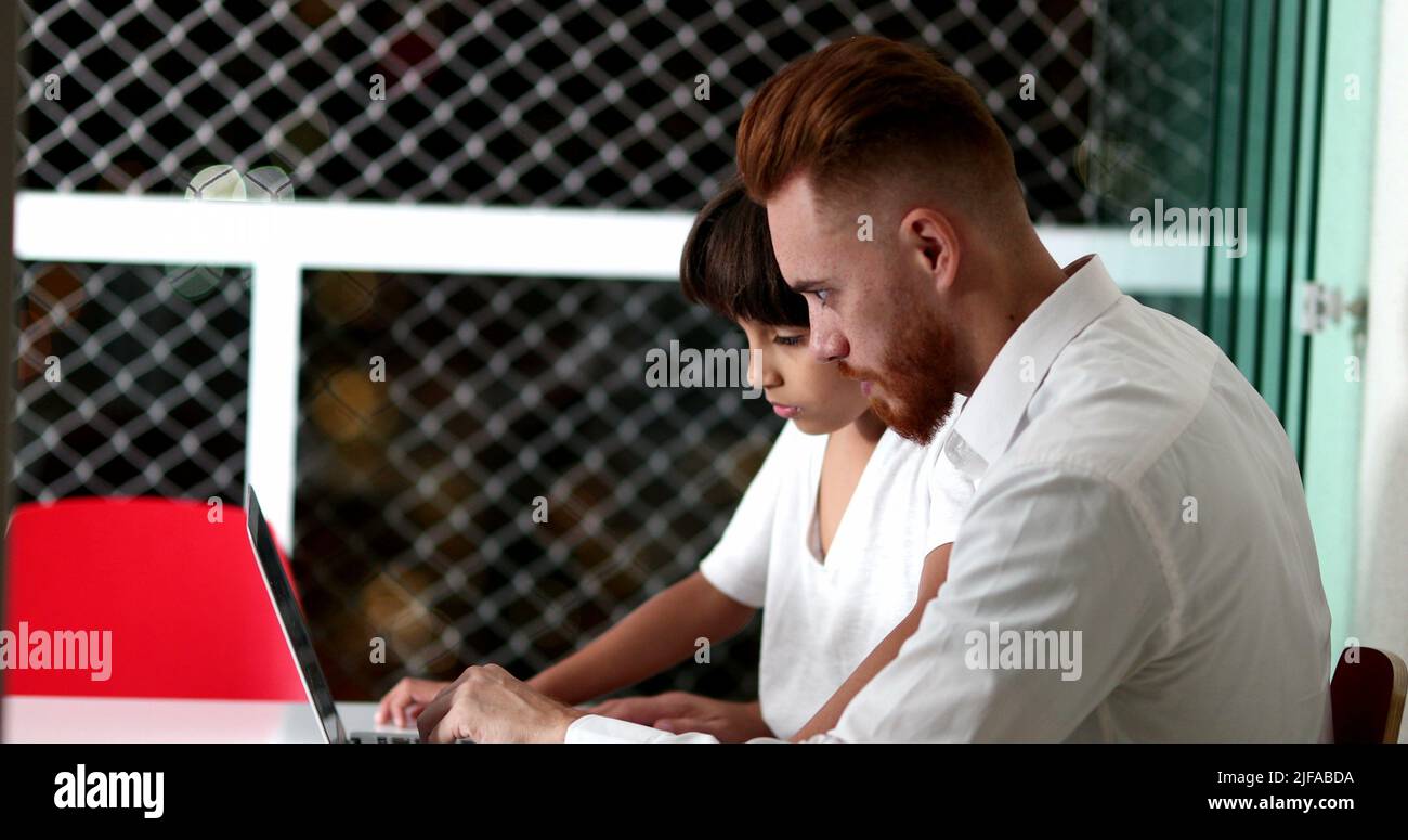 Candid parent and child together in front of computer doing homework at ...