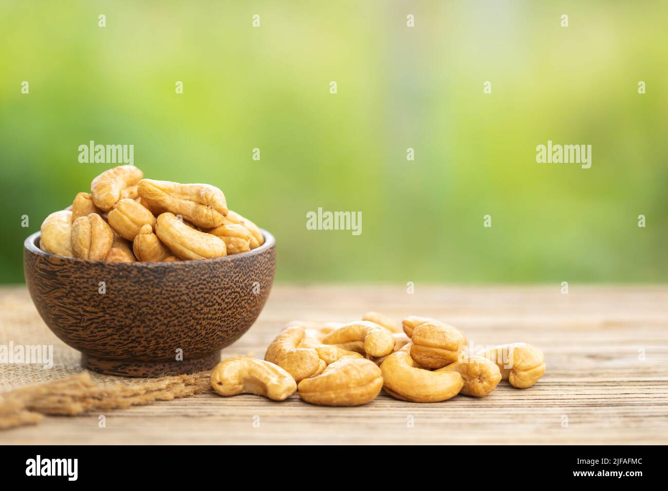 Macro pile of roasted cashew nut in bowl on the table. Blur green ...