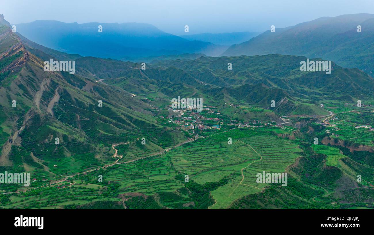 foggy highland valley with vliiage and fields between mountain peaks ...