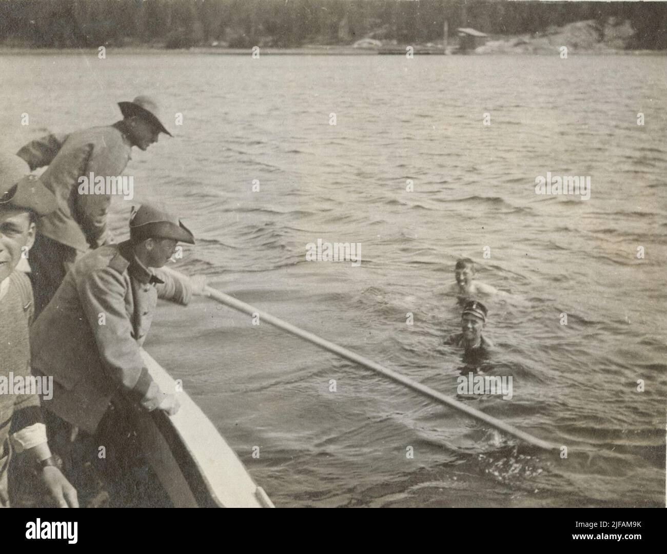Two soldiers swim next to a boat. In the boat there are other soldiers ...