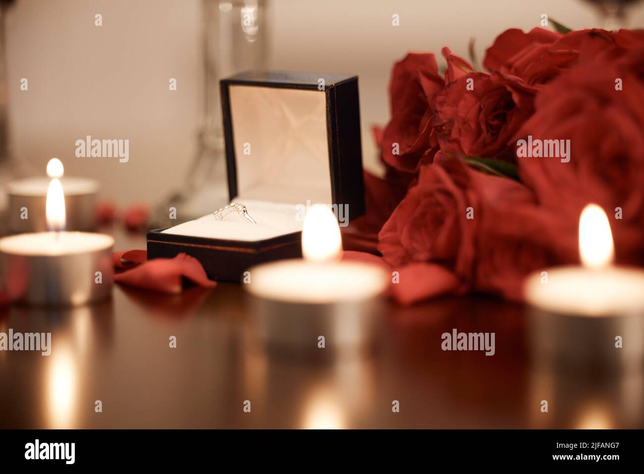 Closeup of romantic engagement ring box, fresh red roses and candles in ...