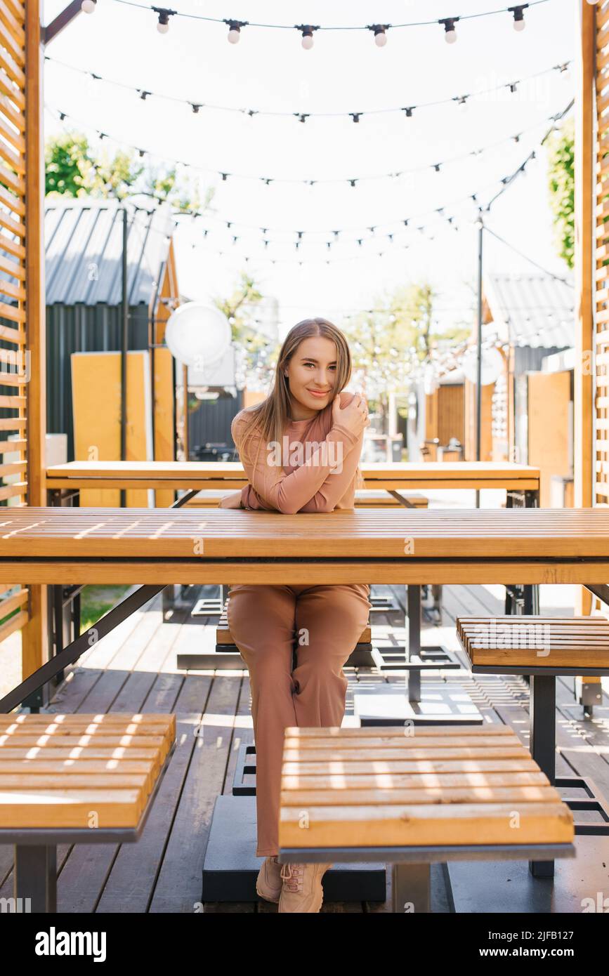 A smiling young attractive woman poses sitting at a table of an outdoor ...