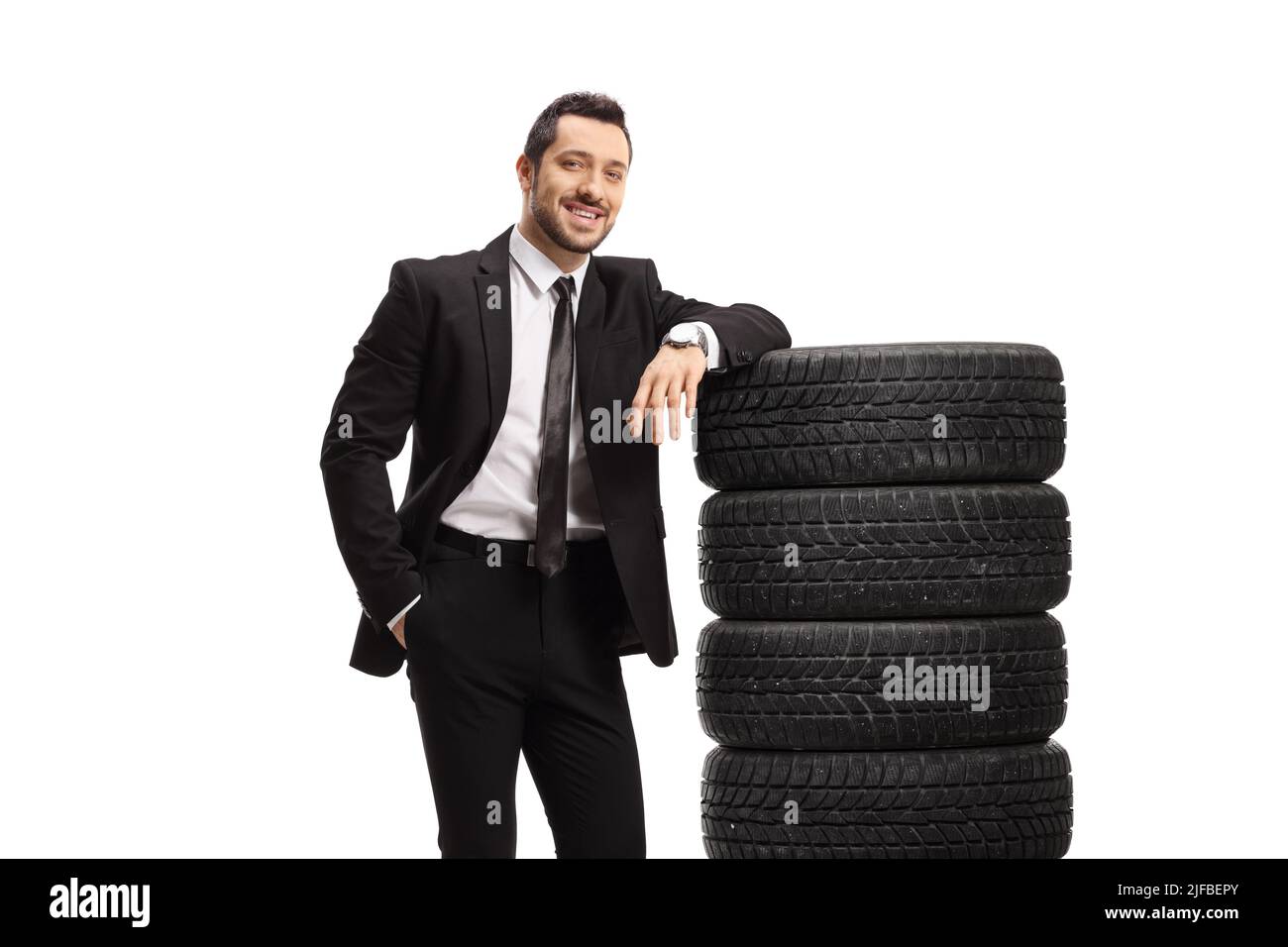 Man in a suit and tie leaning on a pile of car tires isolated on white ...