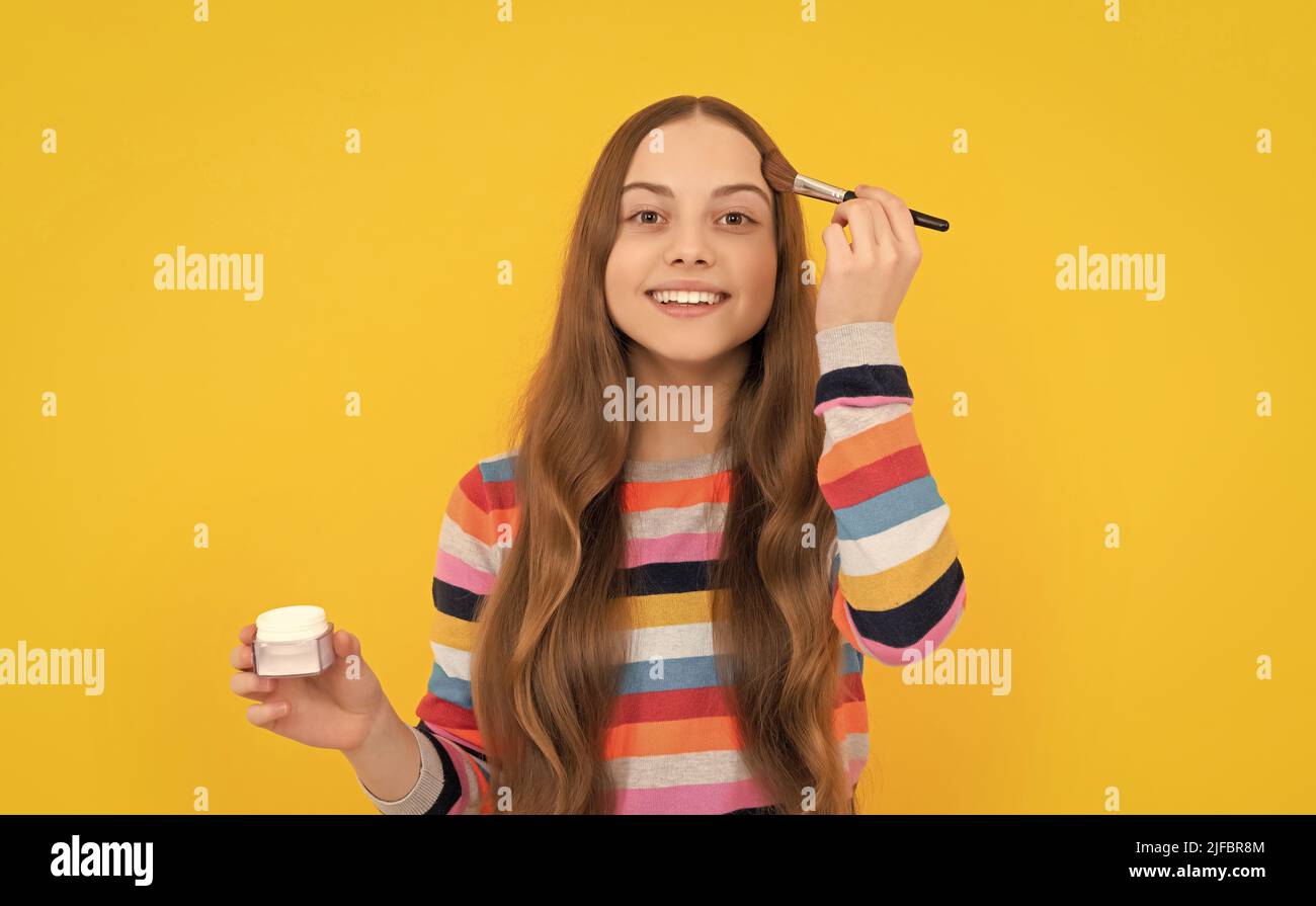 Happy girl child apply foundation with powder brush yellow background ...
