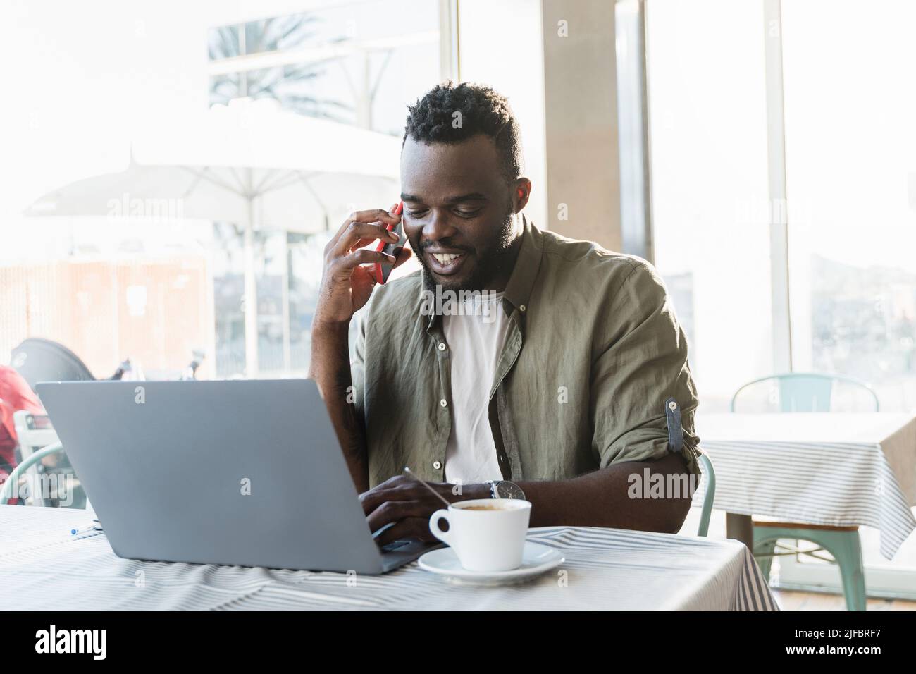 Young african freelancer man working at coffee bar with laptop computer ...