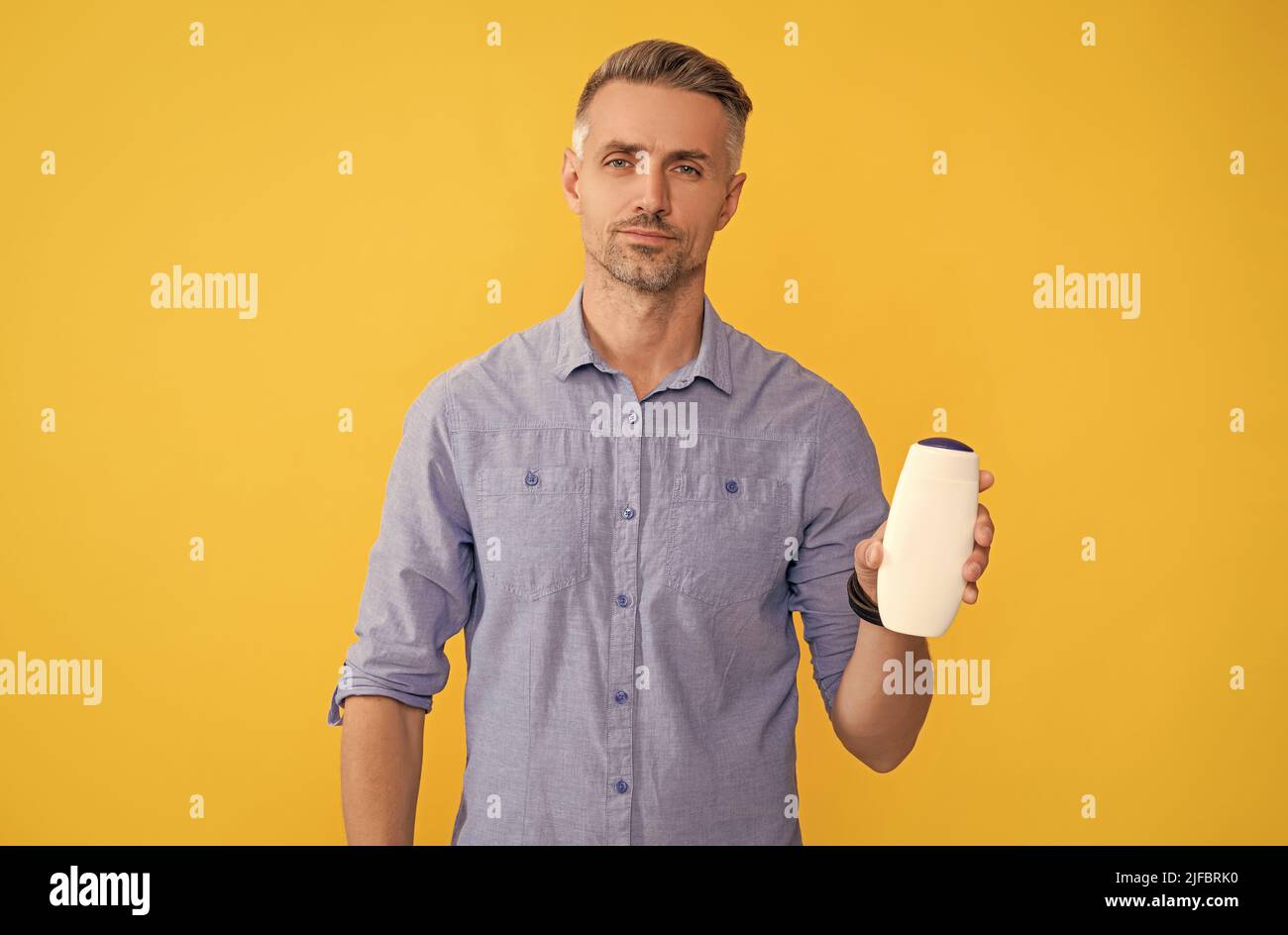 guy showing hair conditioner on yellow background, advertisement Stock ...