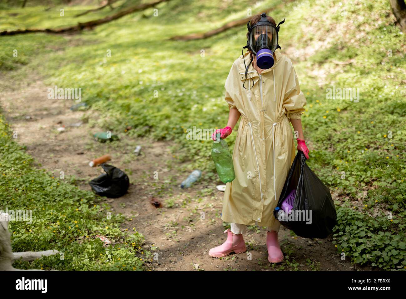 Woman in gas mask and protective clothes collecting scattered plastic ...