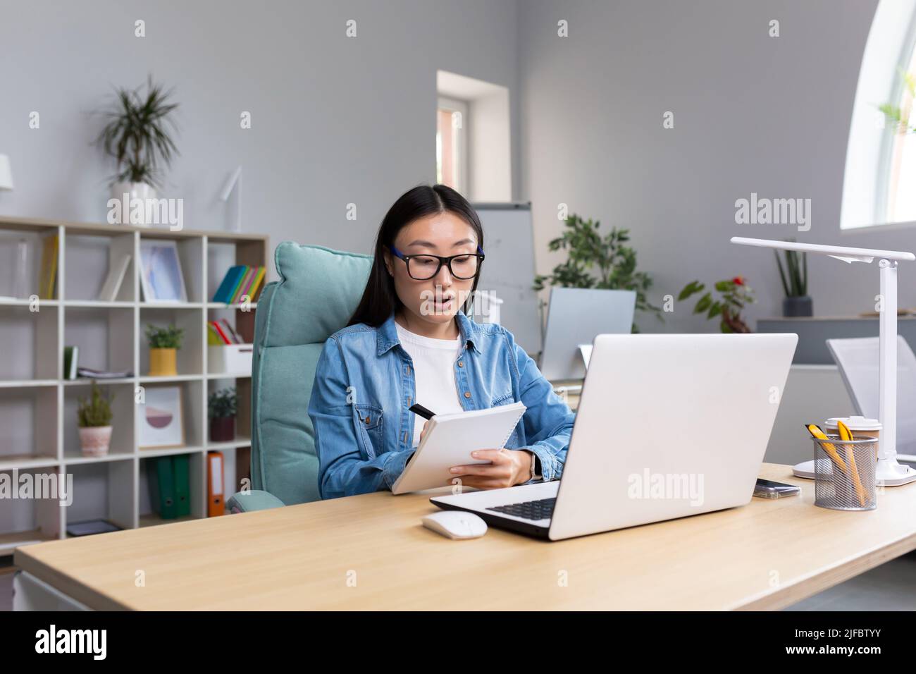 Young Asian woman studying online while sitting in office, writing ...