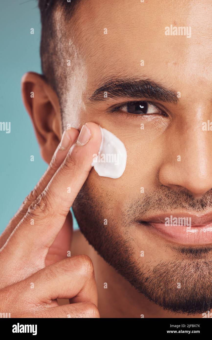 Closeup of one young indian man applying moisturiser lotion to his face ...