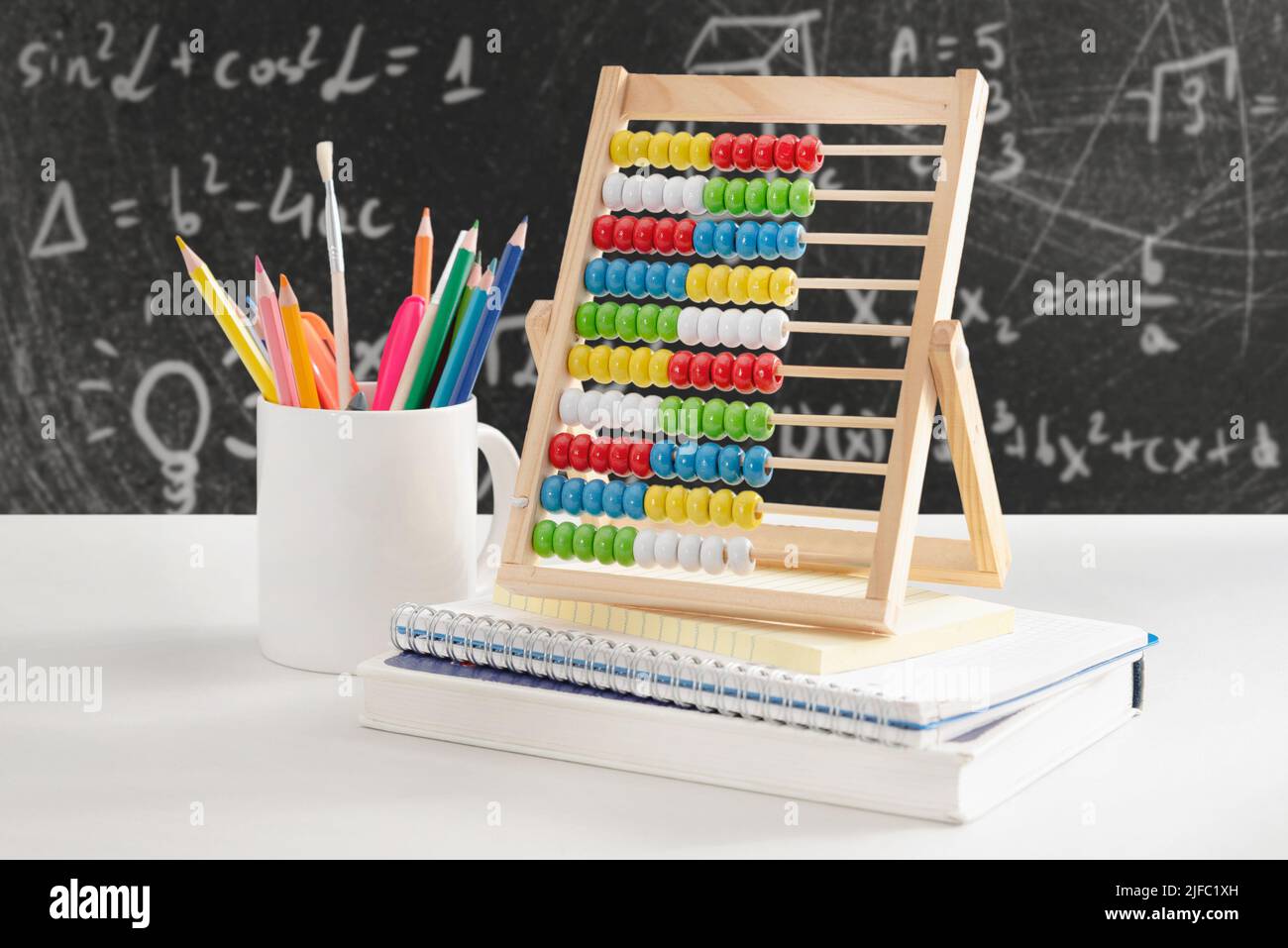 Crayons in mug, abacus and notebooks on school teacher's desk. Blackboard in background Stock ...