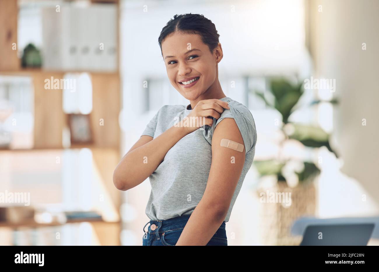Young happy mixed race woman showing a bandaid on her arm after getting ...