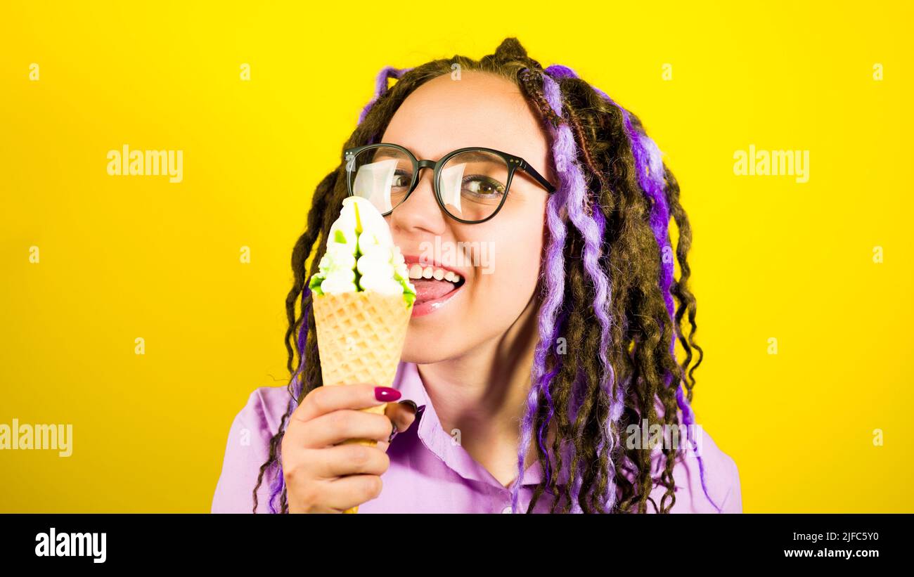 Young woman licking ice cream on yellow background. Portrait of happy ...