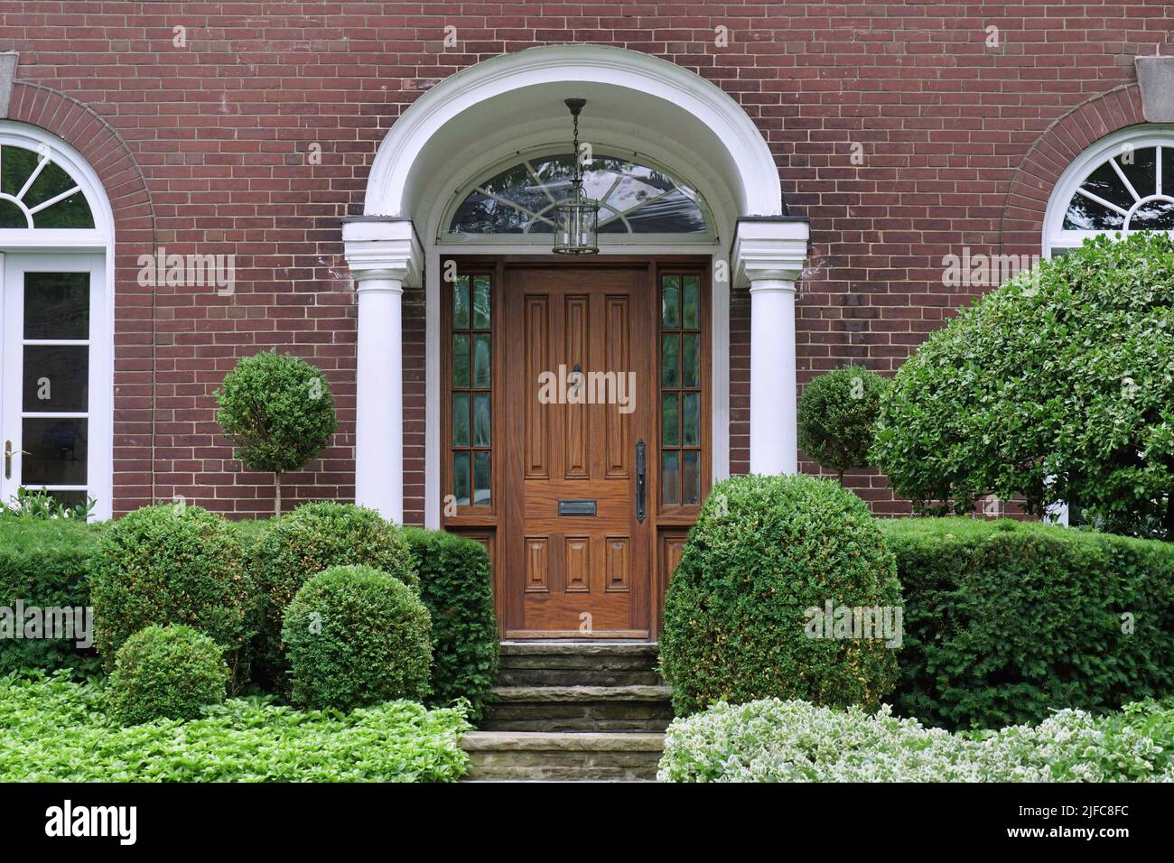 Portico entrance of traditional brick house surrounded by shrubbery ...