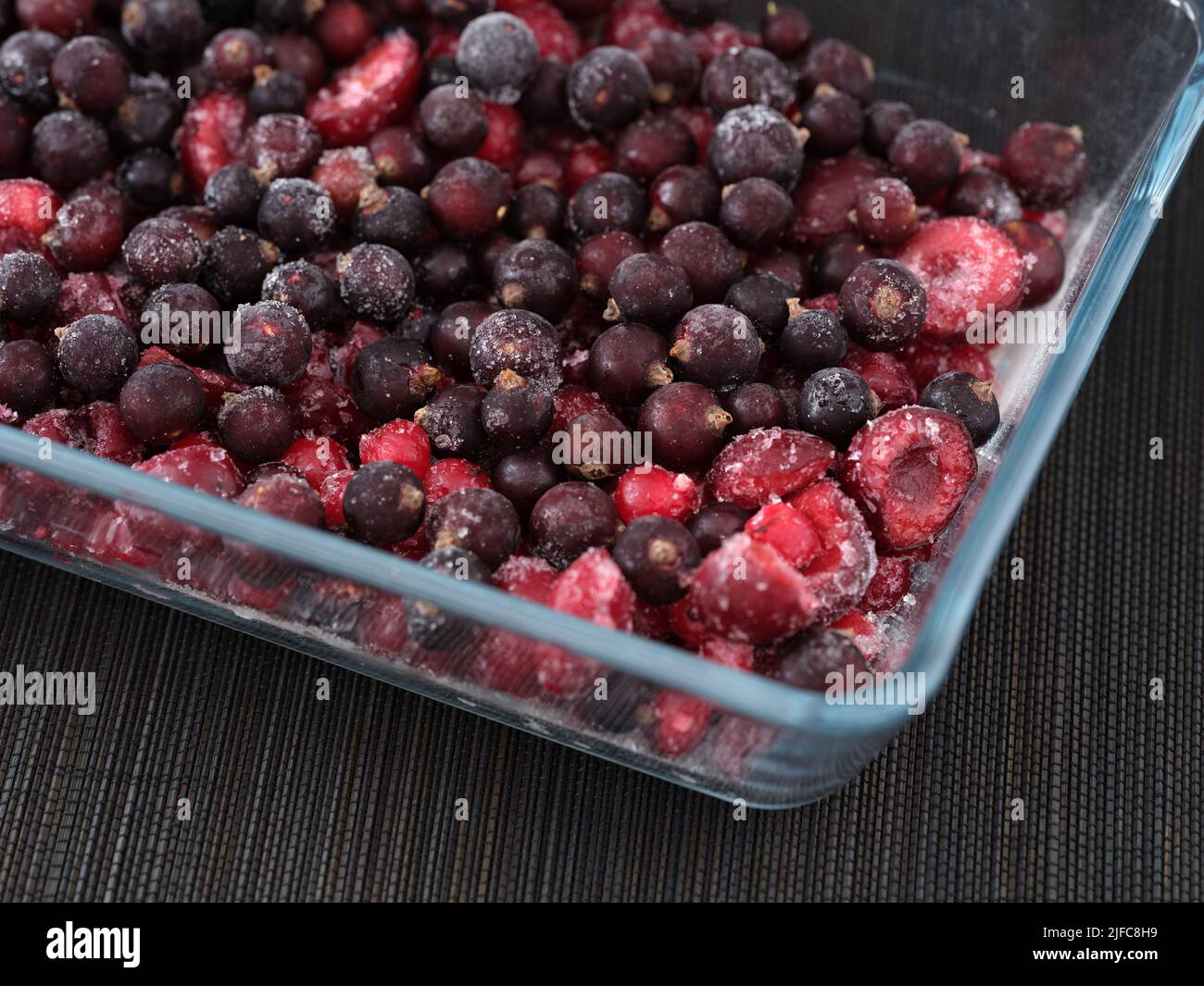Frozen black and red currants with cherries in a glass container. Close ...