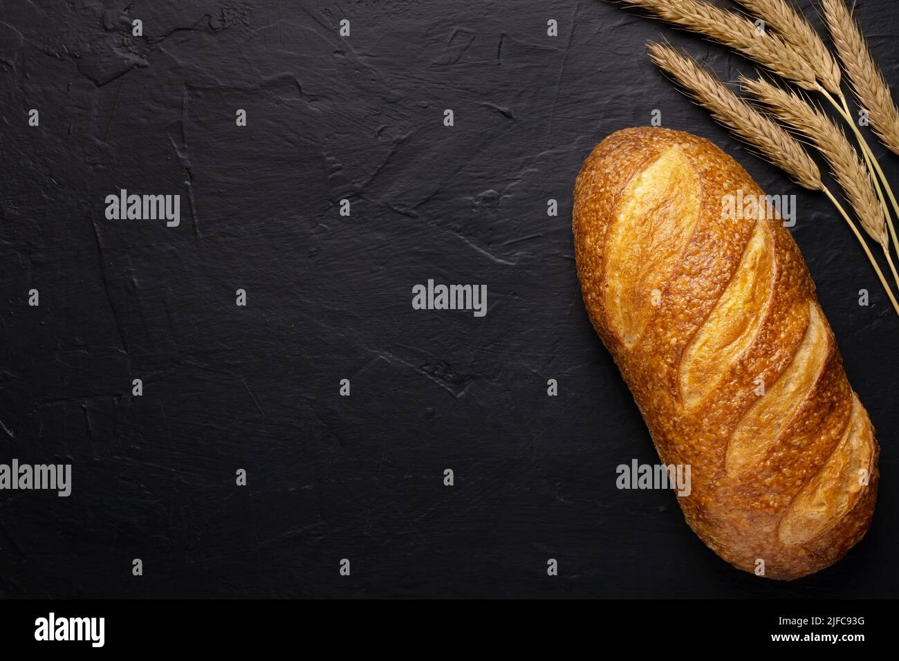 Fresh wheaten baton bread and flour on dark background.Top view. Copy ...