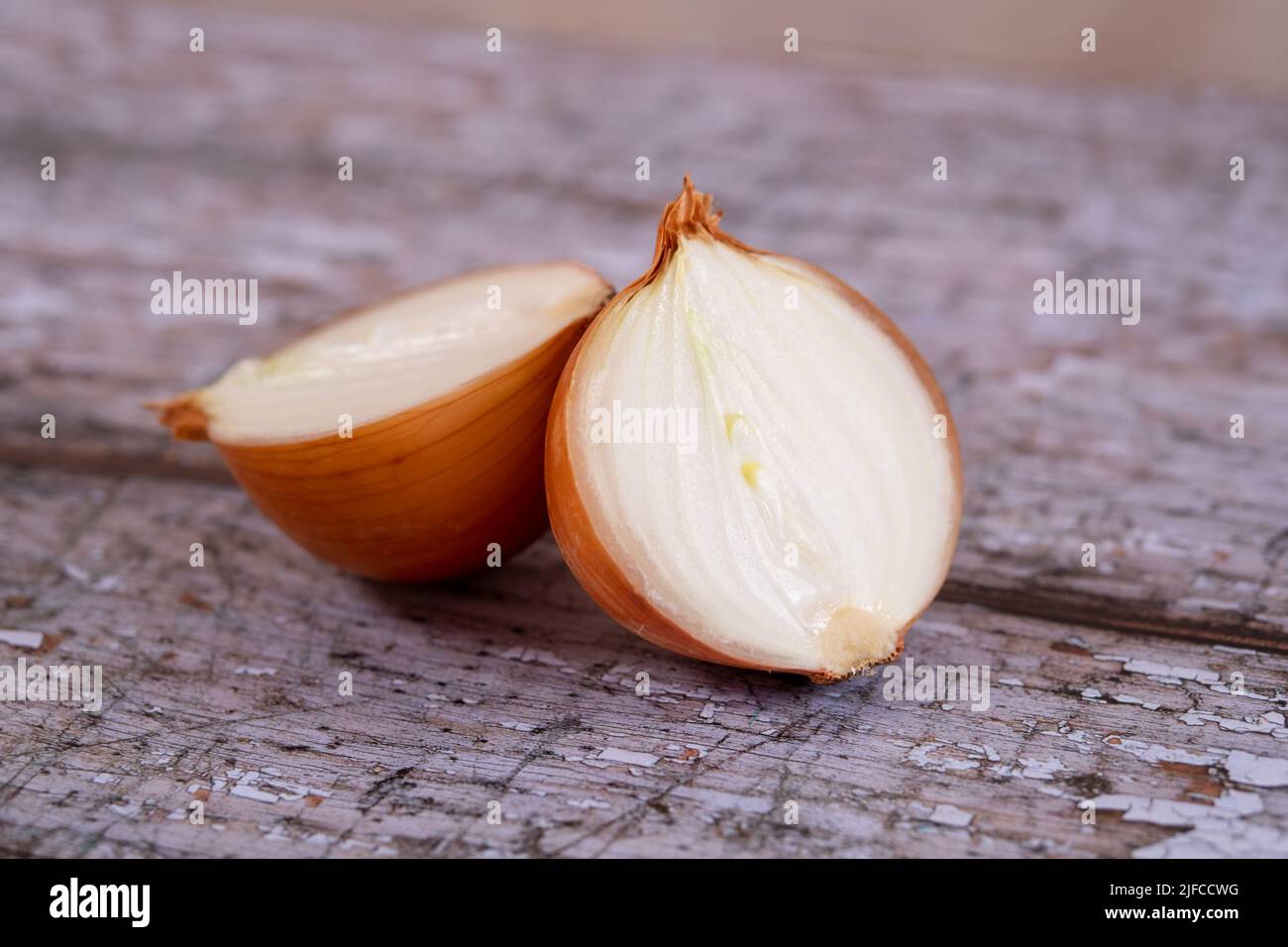 A halved white onion with skin on, against a wooden table top surface ...