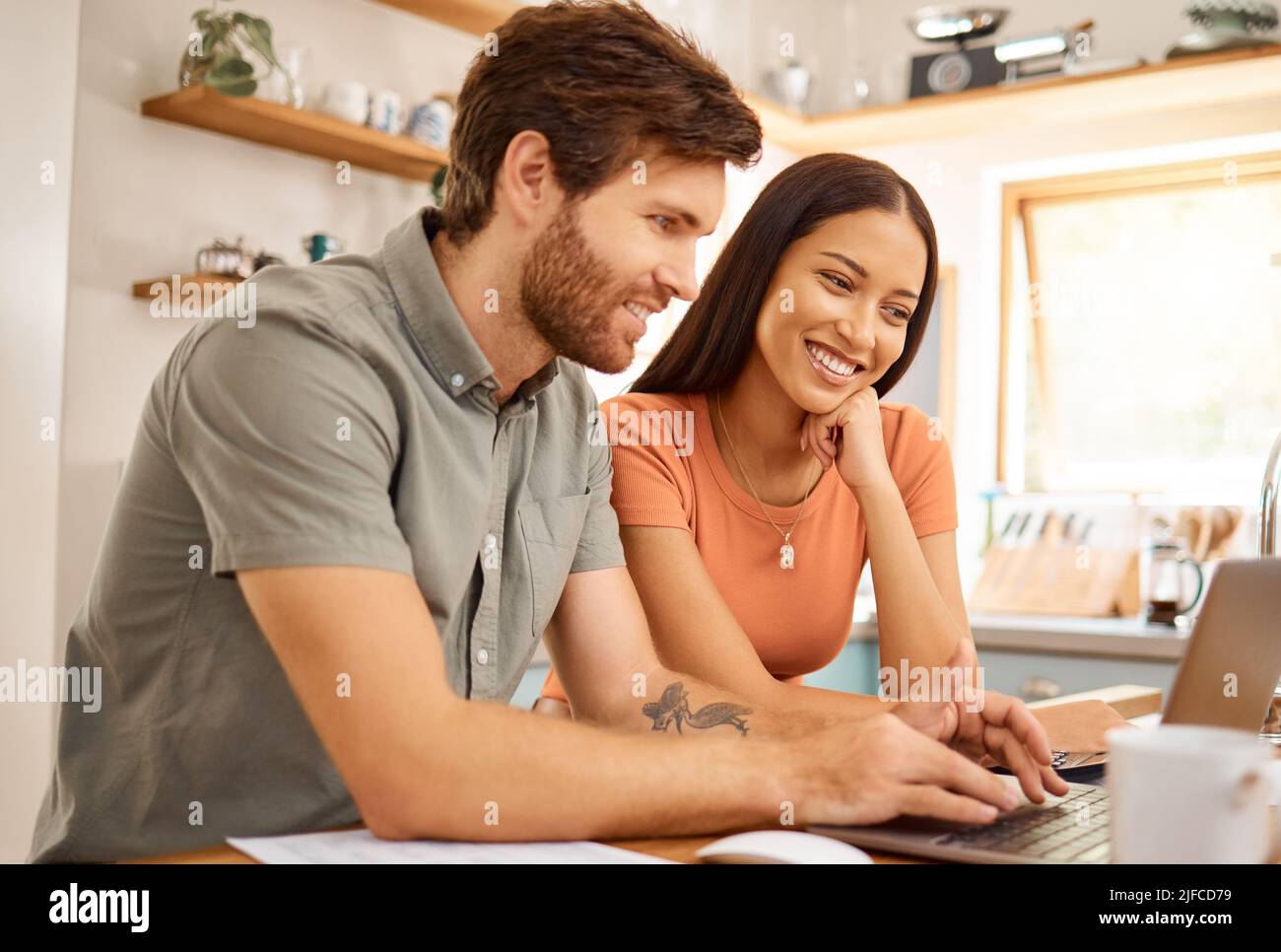 Young happy interracial couple bonding while typing on a laptop ...