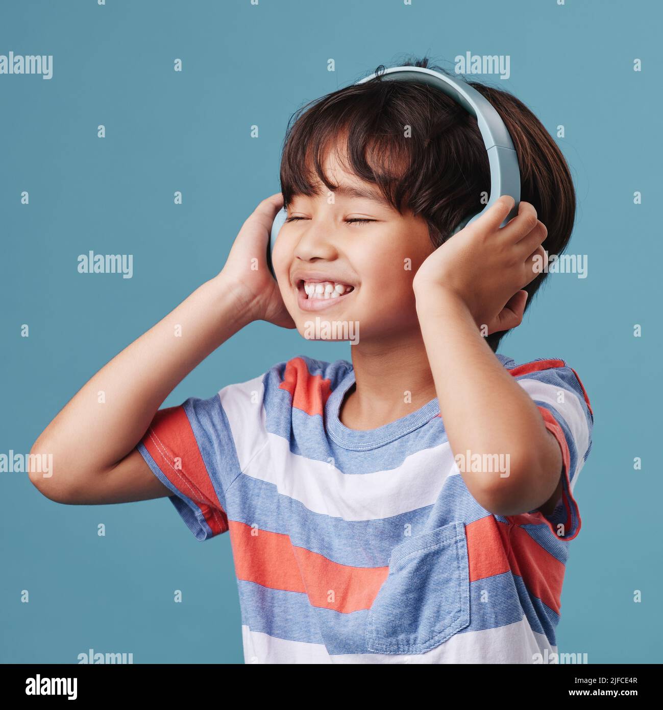 A cute young asian boy enjoying listening to music from his headphones ...