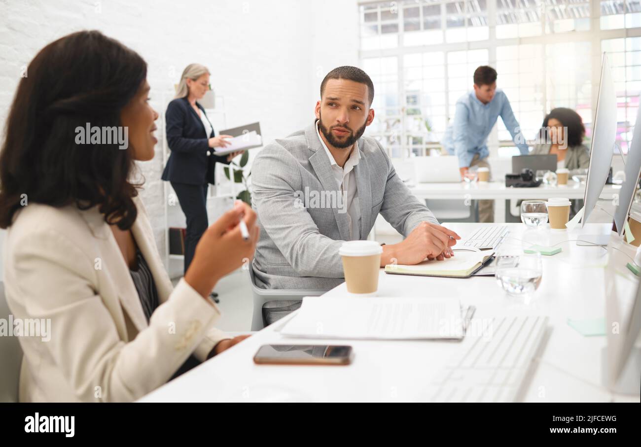 Young diverse colleagues talking while working on desktop computers ...