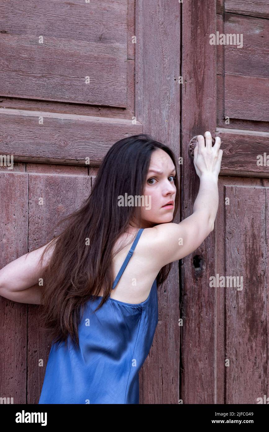 Scared girl opening a wooden door Stock Photo - Alamy