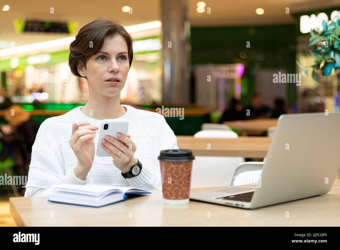 young woman working on a laptop typing something in a mobile phone ...