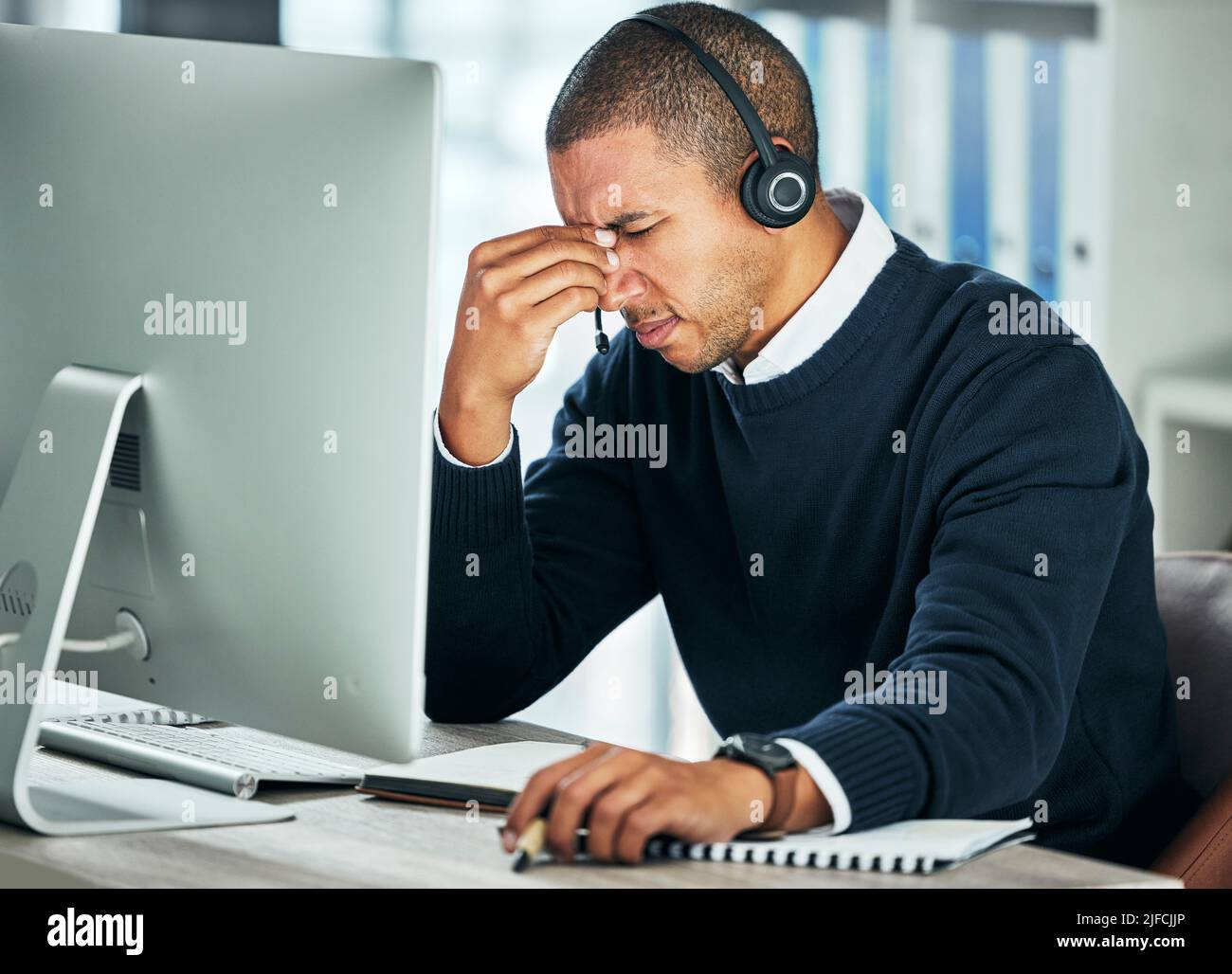Stressed male call centre agent getting a headache while working on ...