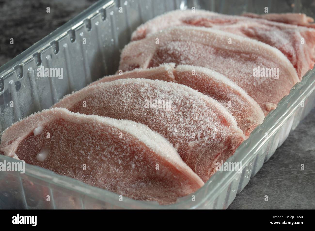 Frozen pork chops in plastic tray packaging thawing. On a concrete ...