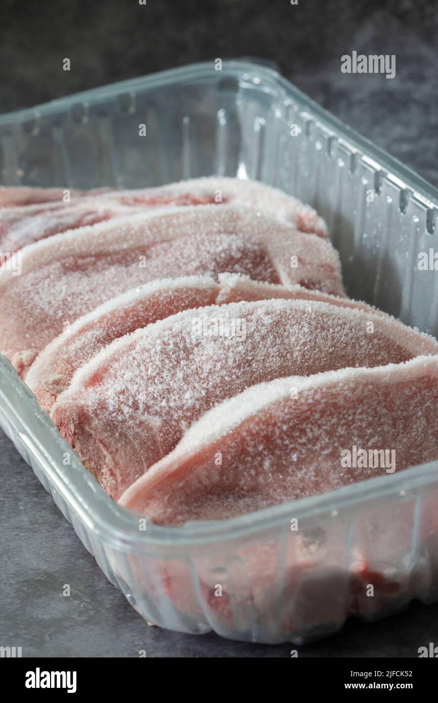Frozen pork chops in plastic tray packaging thawing. On a concrete ...