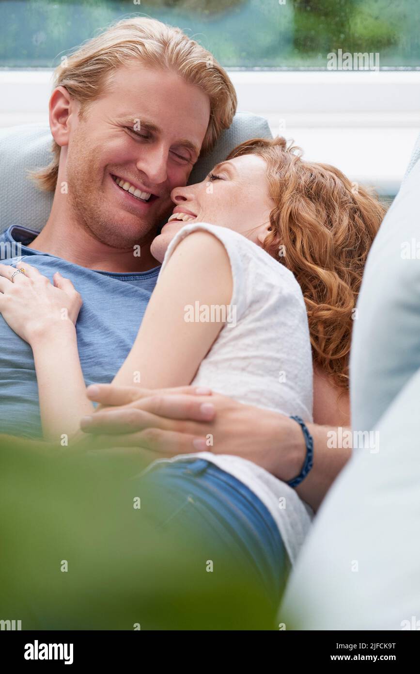 A content young couple happily snuggling while lying on the couch. A ...